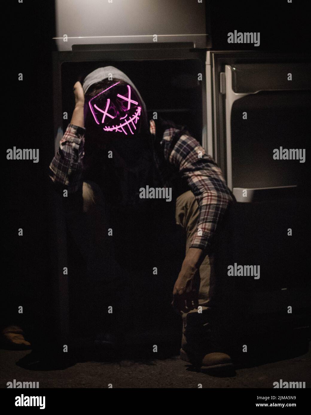 A vertical shot of a young boy in a fridge wearing led glow purge mask ...