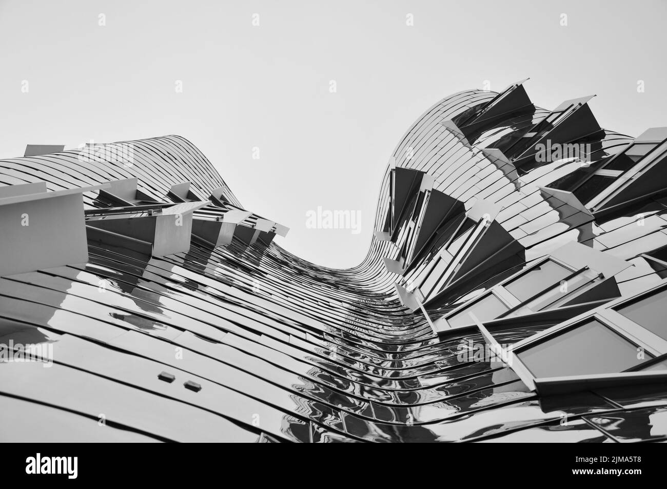 A monochrome, low-angle shot of the mirrored facade of the Gehry ...