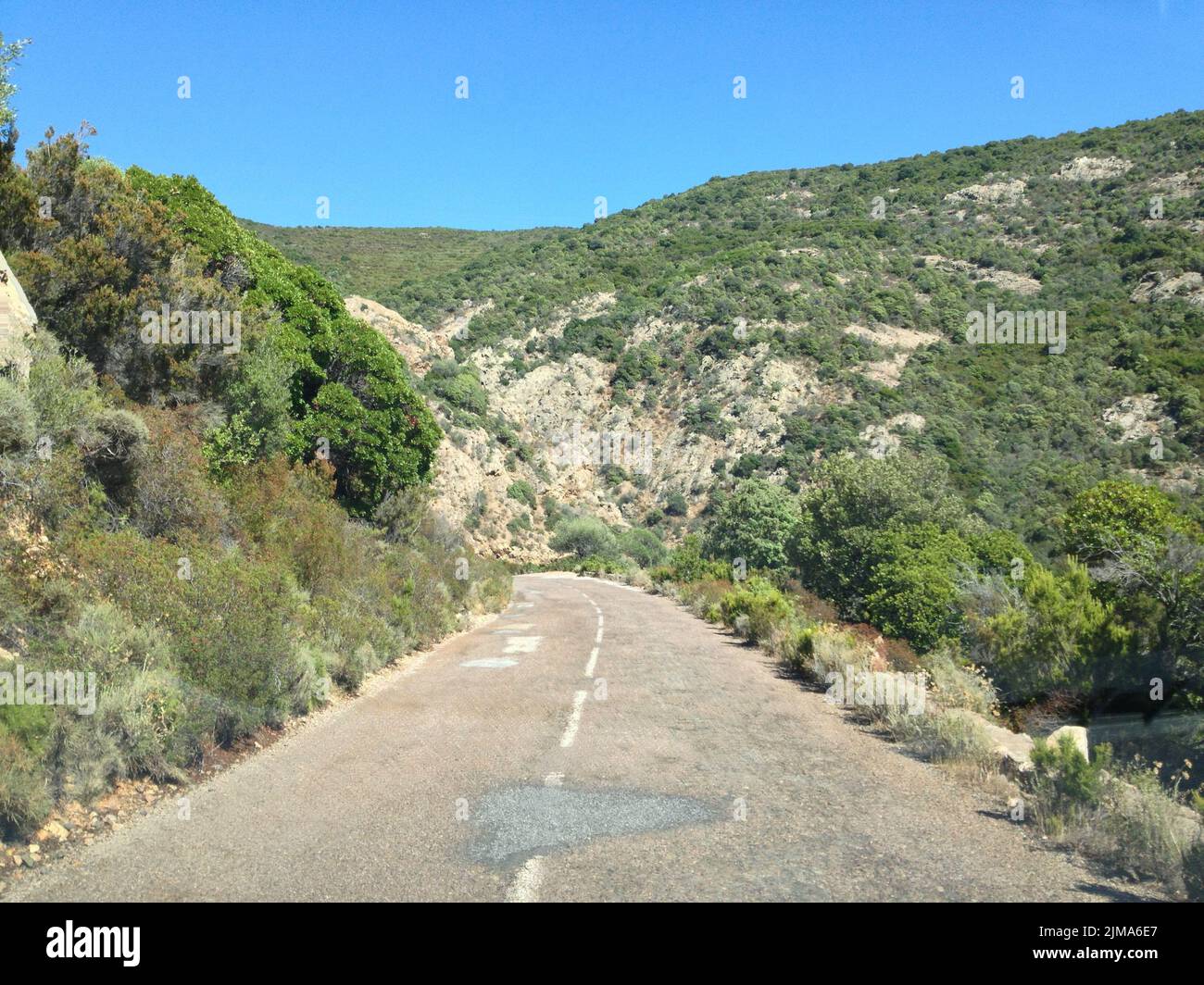 An asphalt road with a lane marking in between two hills covered with ...