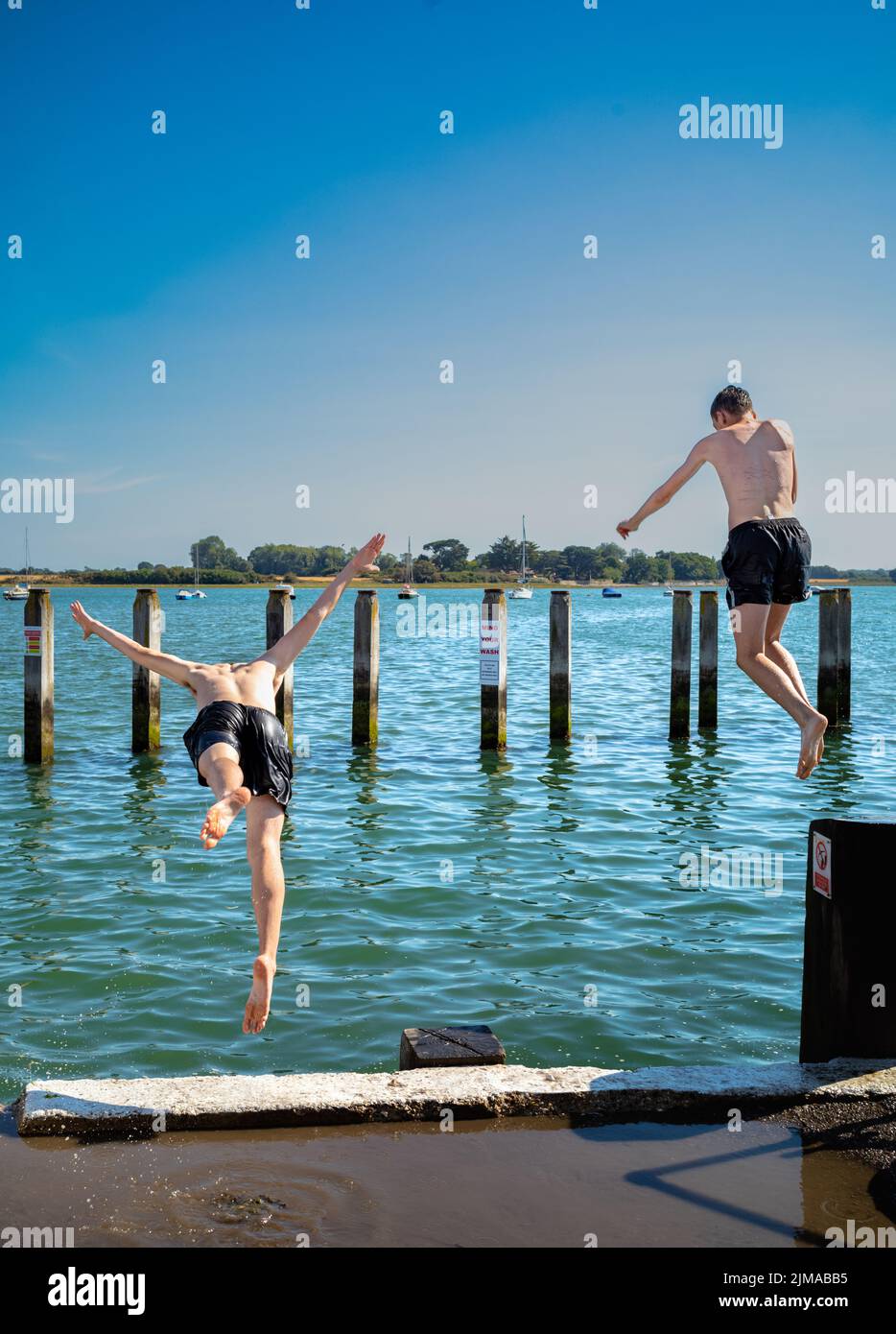 Two teenage boys dive into the sea at high tide at Bosham, England ...
