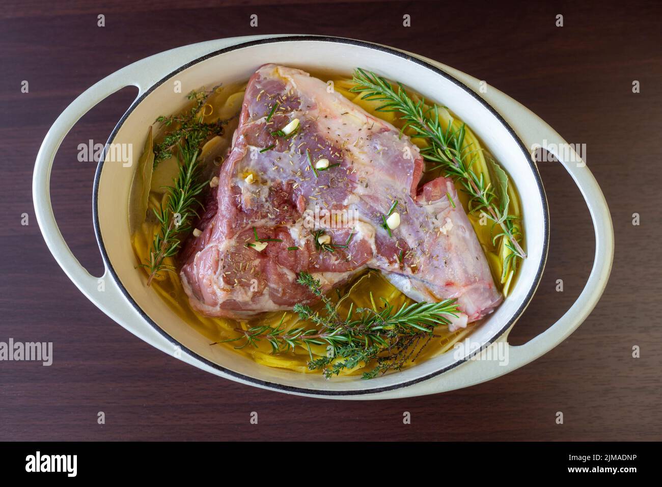 raw leg of lamb prepared to cook with sliced potatoes and provencal ...