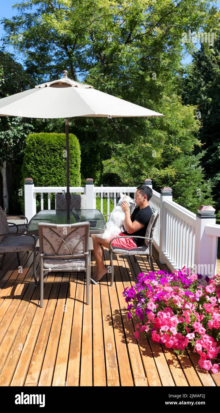 Young man giving hug to his dog while working from home on his cedar ...