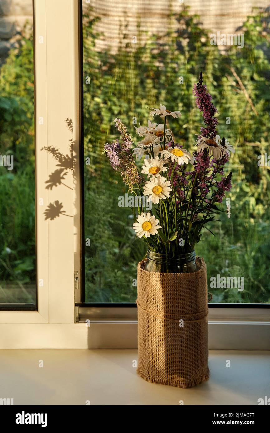 Bouquet of wild meadow flowers on window sill of rural house in sunset ...