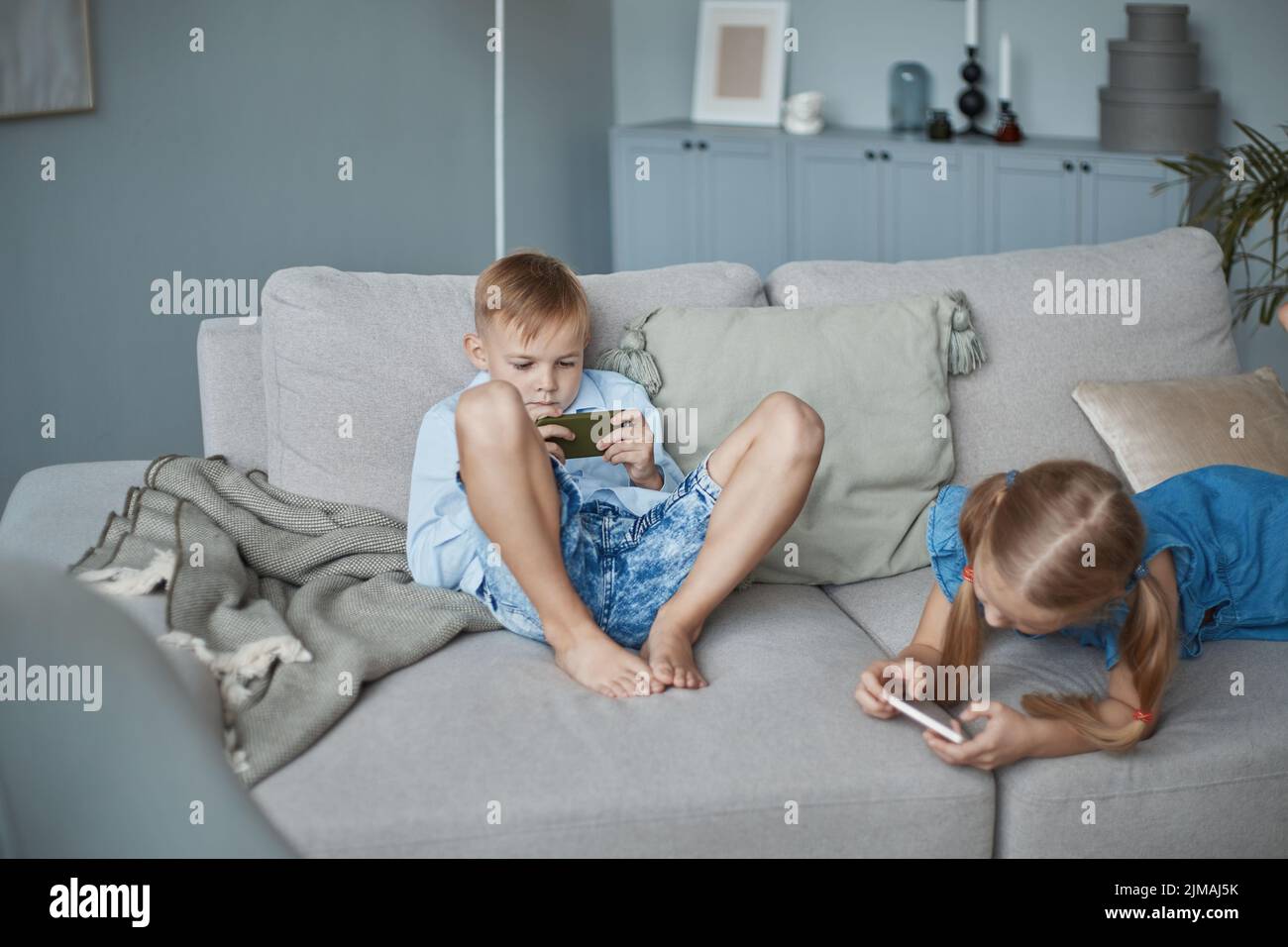 little brother and sister using their smartphones in their free time ...