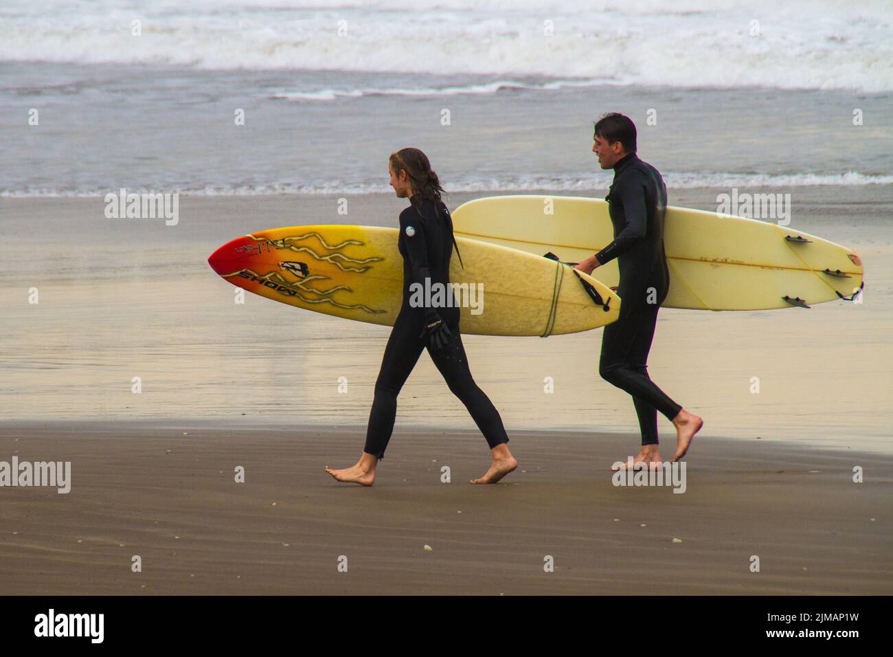 A view of a couple in wetsuits with surfing boards on the beach getting ...