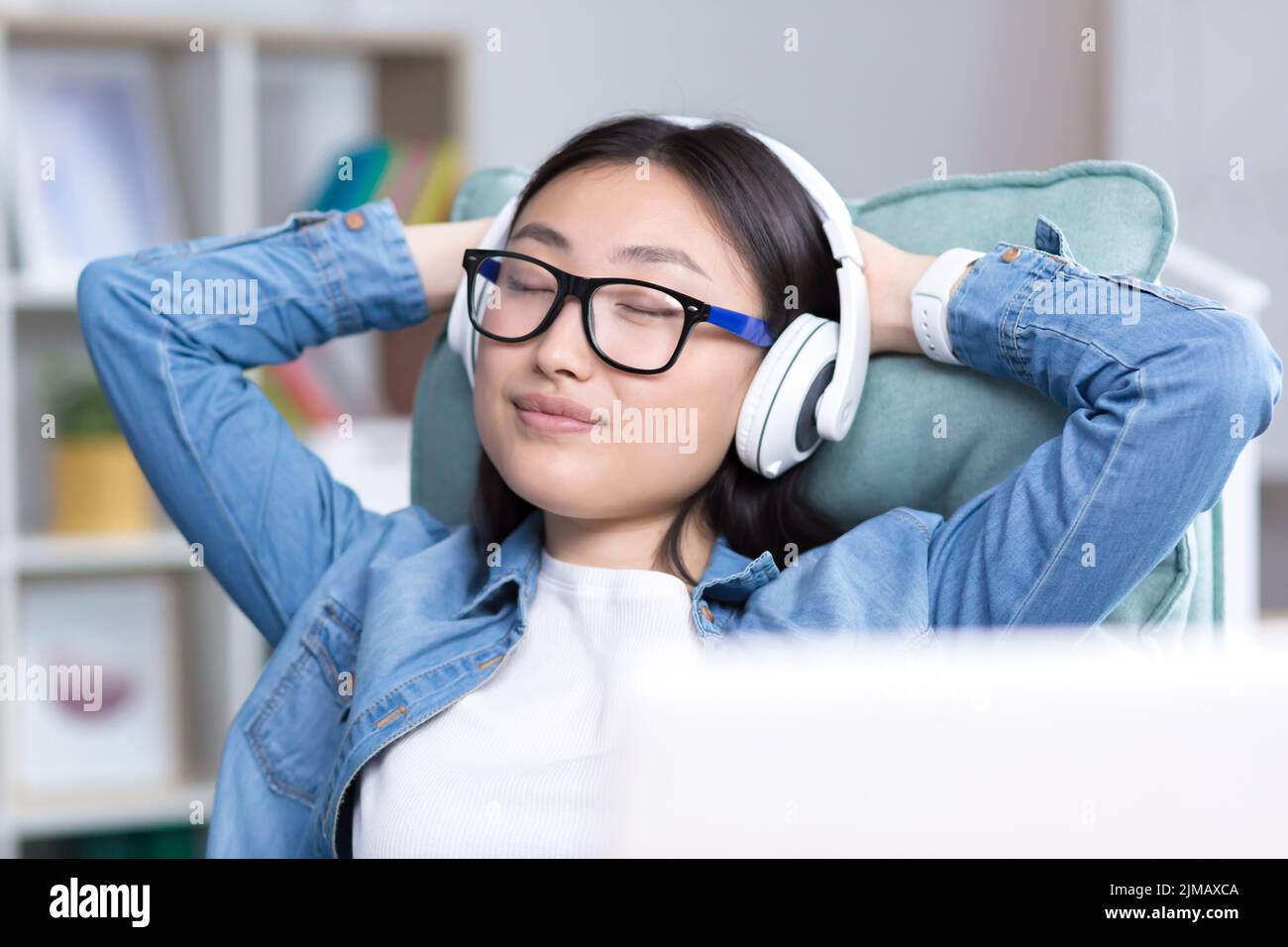 Young beautiful Asian woman listening to music in headphones, closing ...