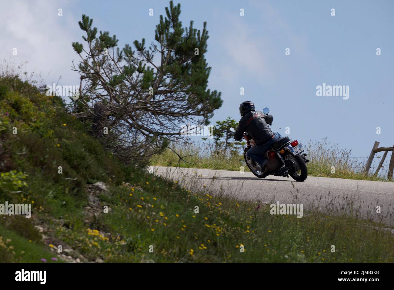 A man in a helmet riding a red vintage Honda CB750 bike on a sunny day ...