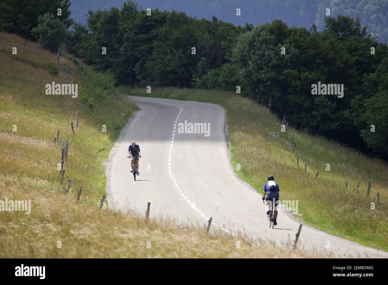 Two people riding bicycles on a curvy asphalt road during the daytime ...