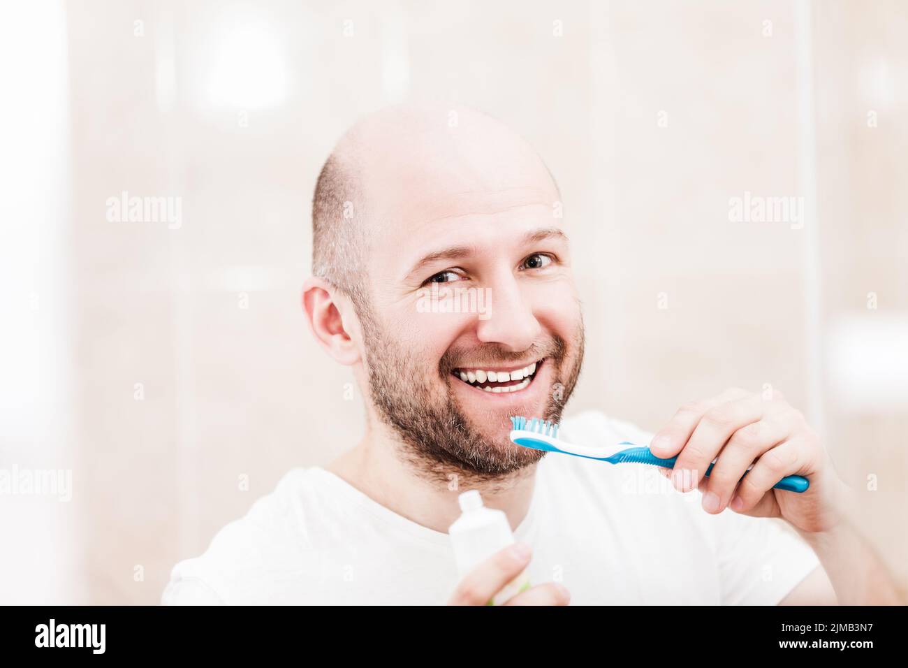 Smiling bald man holding toothbrush with toothpaste and brushing teeth ...