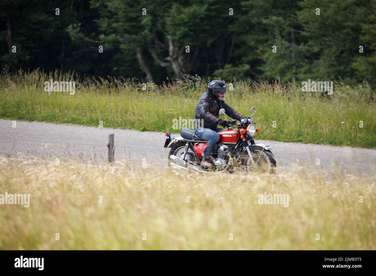 A man in a helmet riding a red vintage Honda CB750 bike on a sunny day ...
