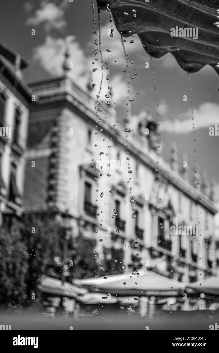 A vertical closeup grayscale shot of water drops overflowing from a ...