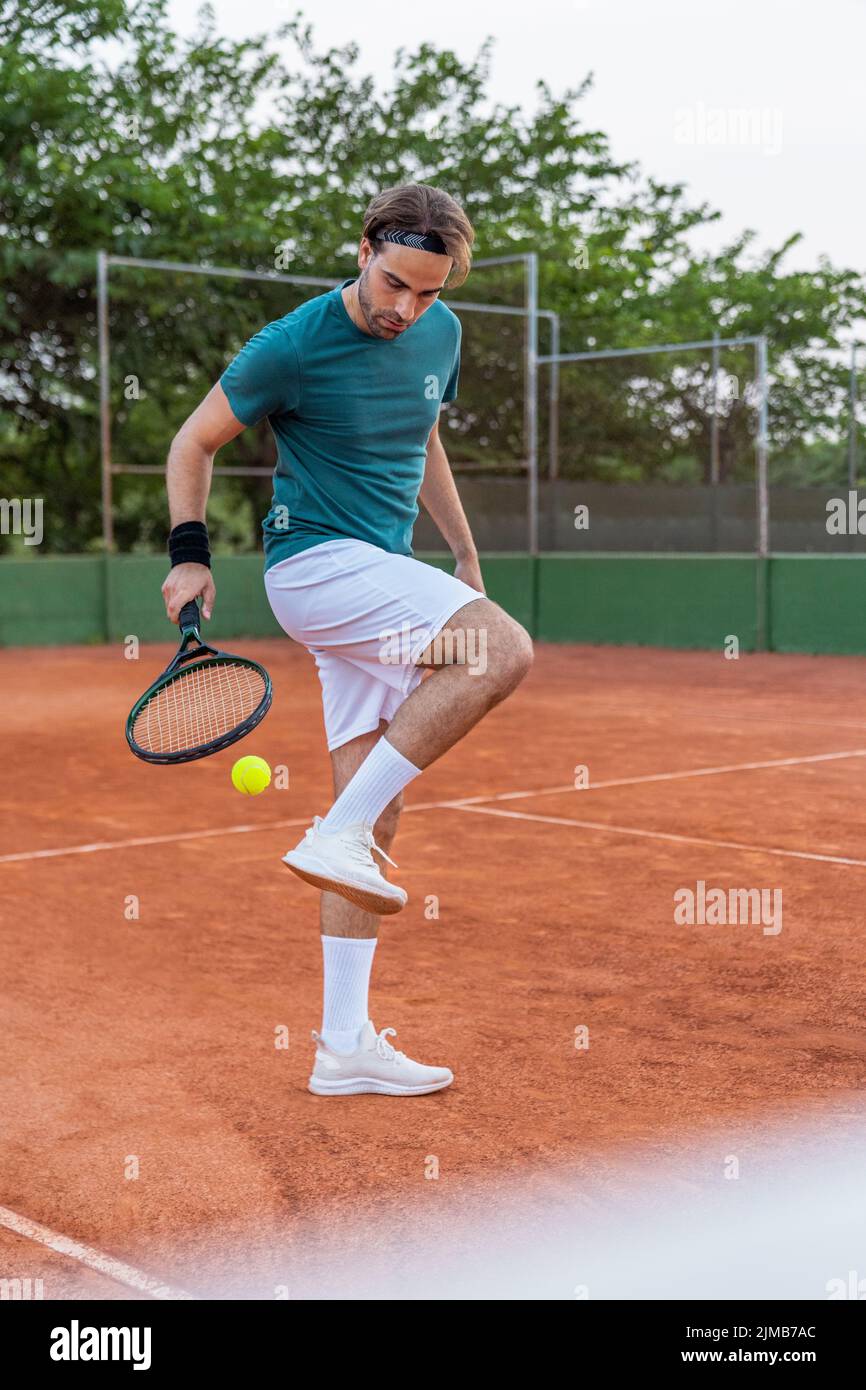 Young caucasian man with long hair picking up the ball from the ground ...