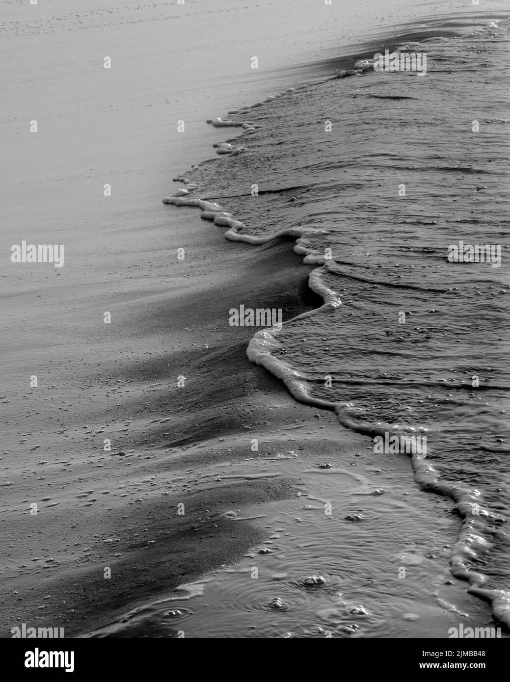 A grayscale of waves on a sandy beach Stock Photo - Alamy