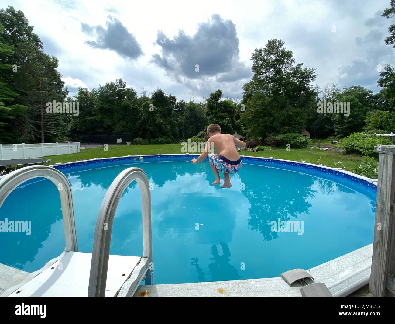 A teenage boy jumping into the swimming pool with trees in the ...