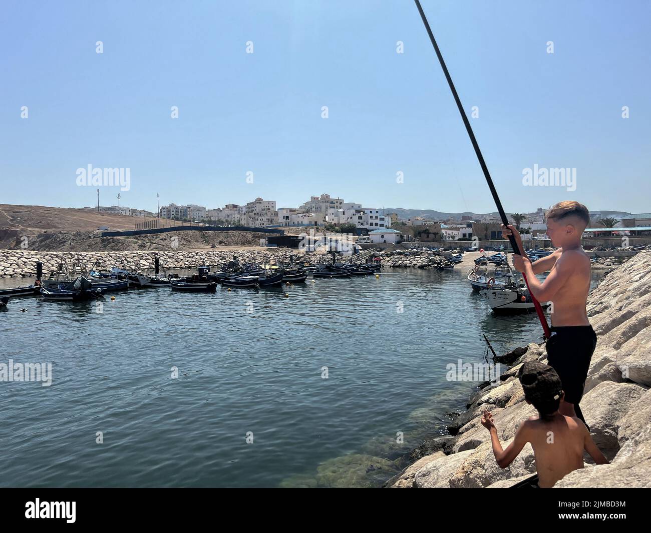 Two kids fishing in a small harbor Stock Photo - Alamy