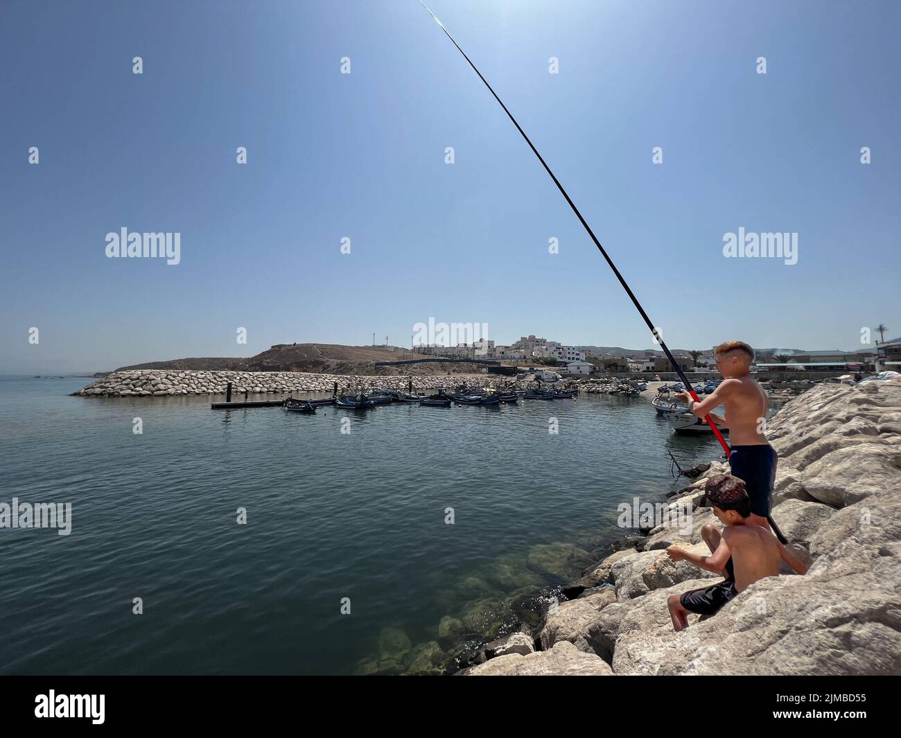 Two kids fishing in a small harbor Stock Photo - Alamy