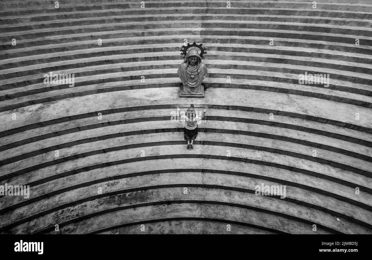 A grayscale top view of a woman on her knees praying in front of a ...