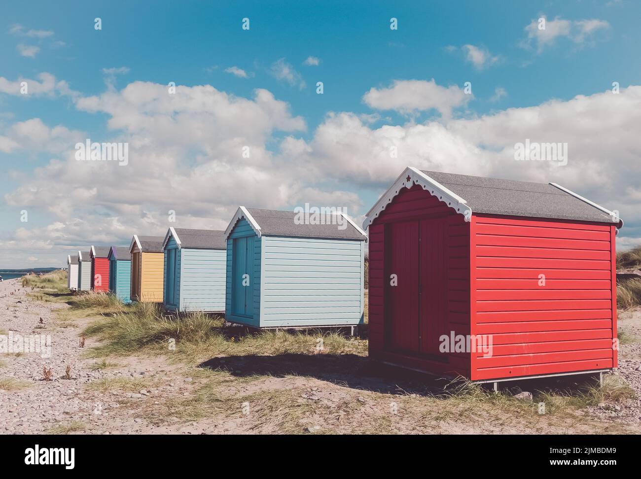 The rows of colorful beach sheds on pebble beach on blue cloudy sky ...