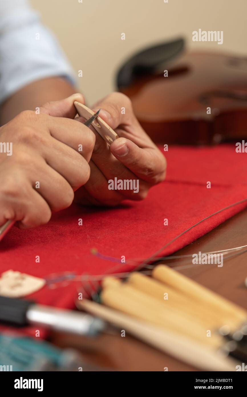 Vertical photo of worker's hands shaping a violin bridge using a small ...