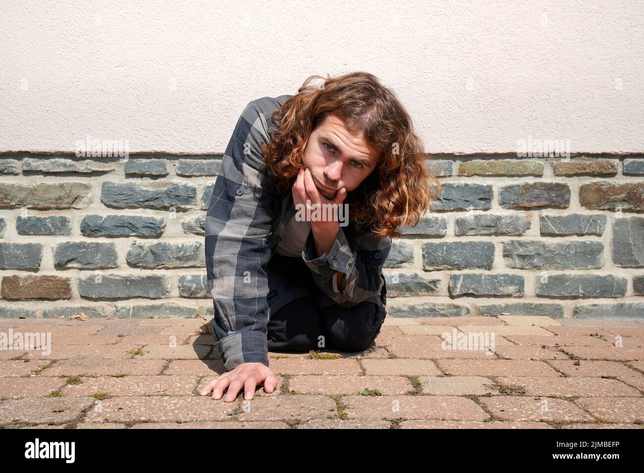 A man with long curly hair sits on his knees with one hand on the ...