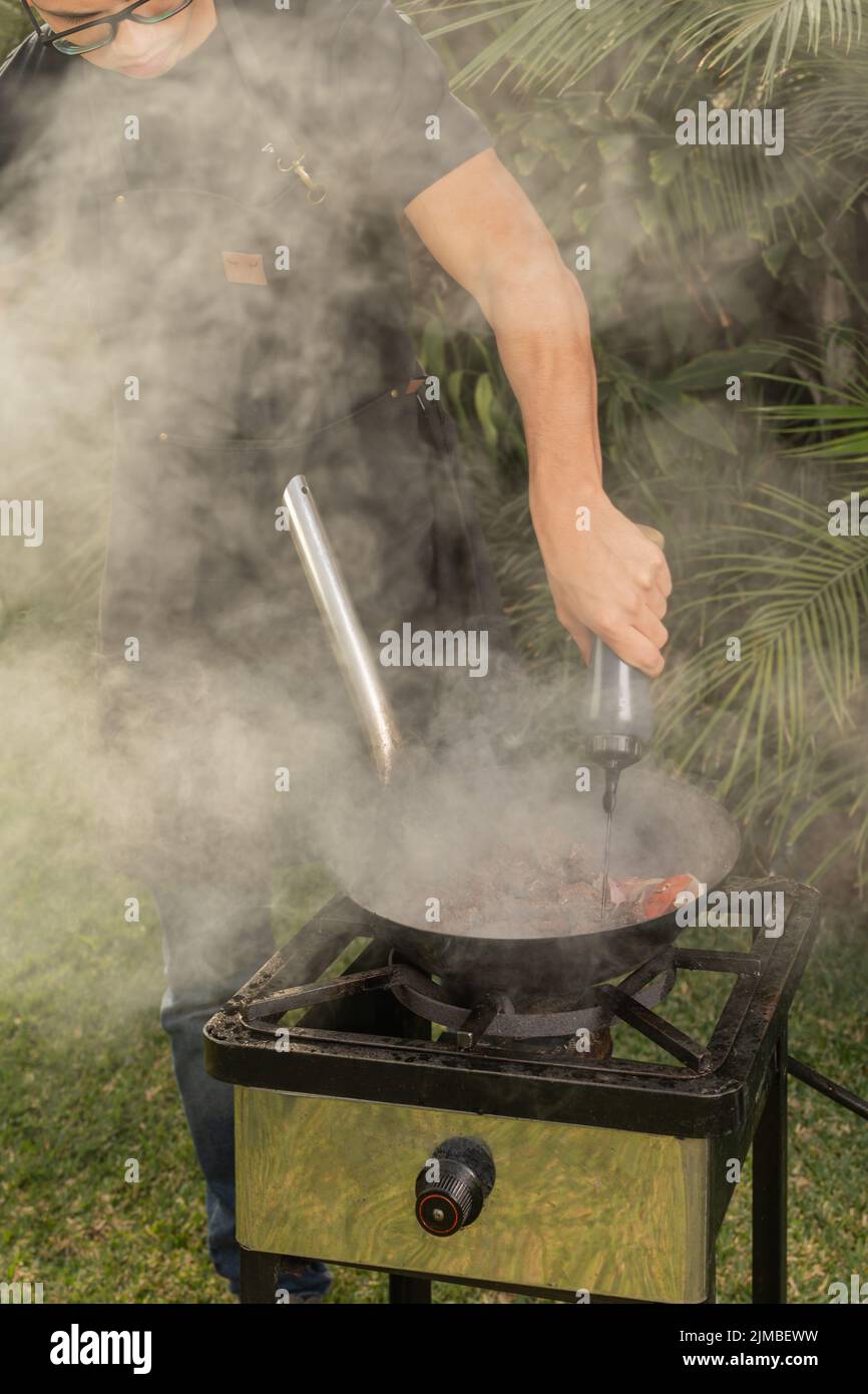Vertical photo of a man seasoning food while cooking in a garden Stock ...