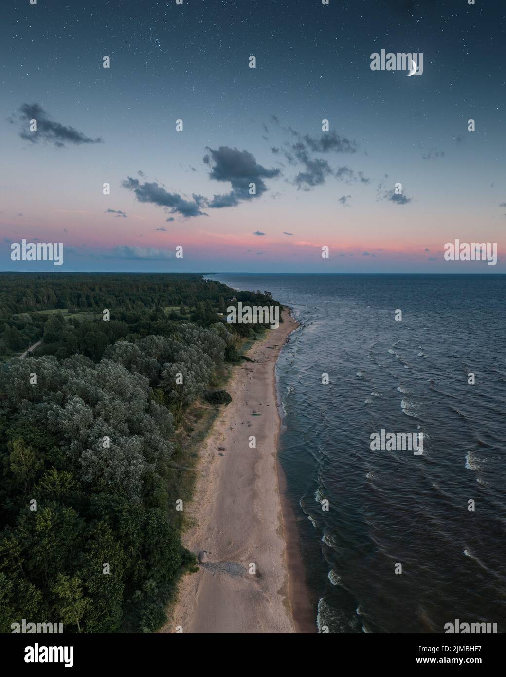 An aerial view of a sandy beach and dense green forest on the twilight ...