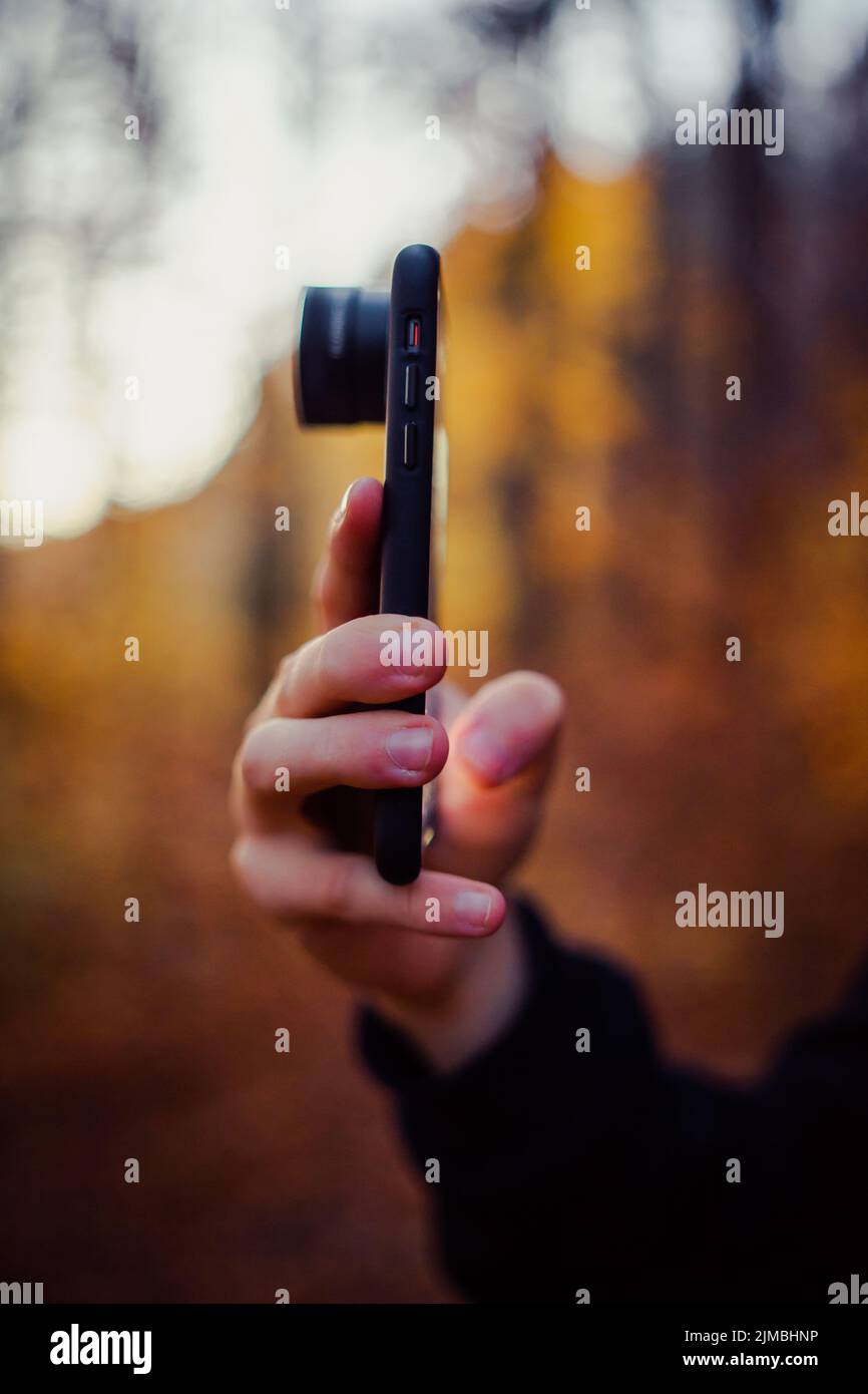 A hand holding a phone with a camera lense in an autumn forest Stock ...