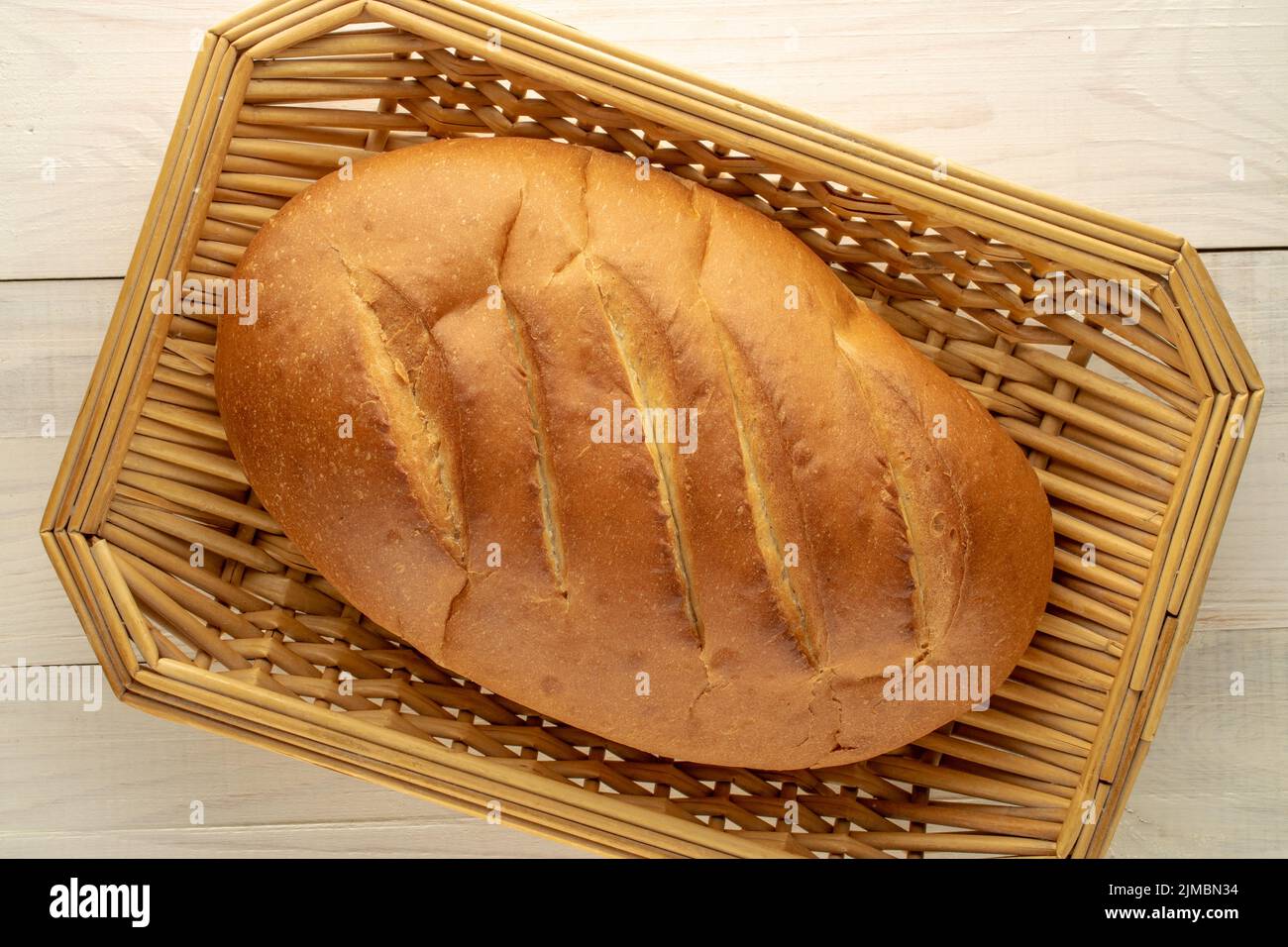 One fragrant fresh loaf with a straw tray on a wooden table, close-up ...