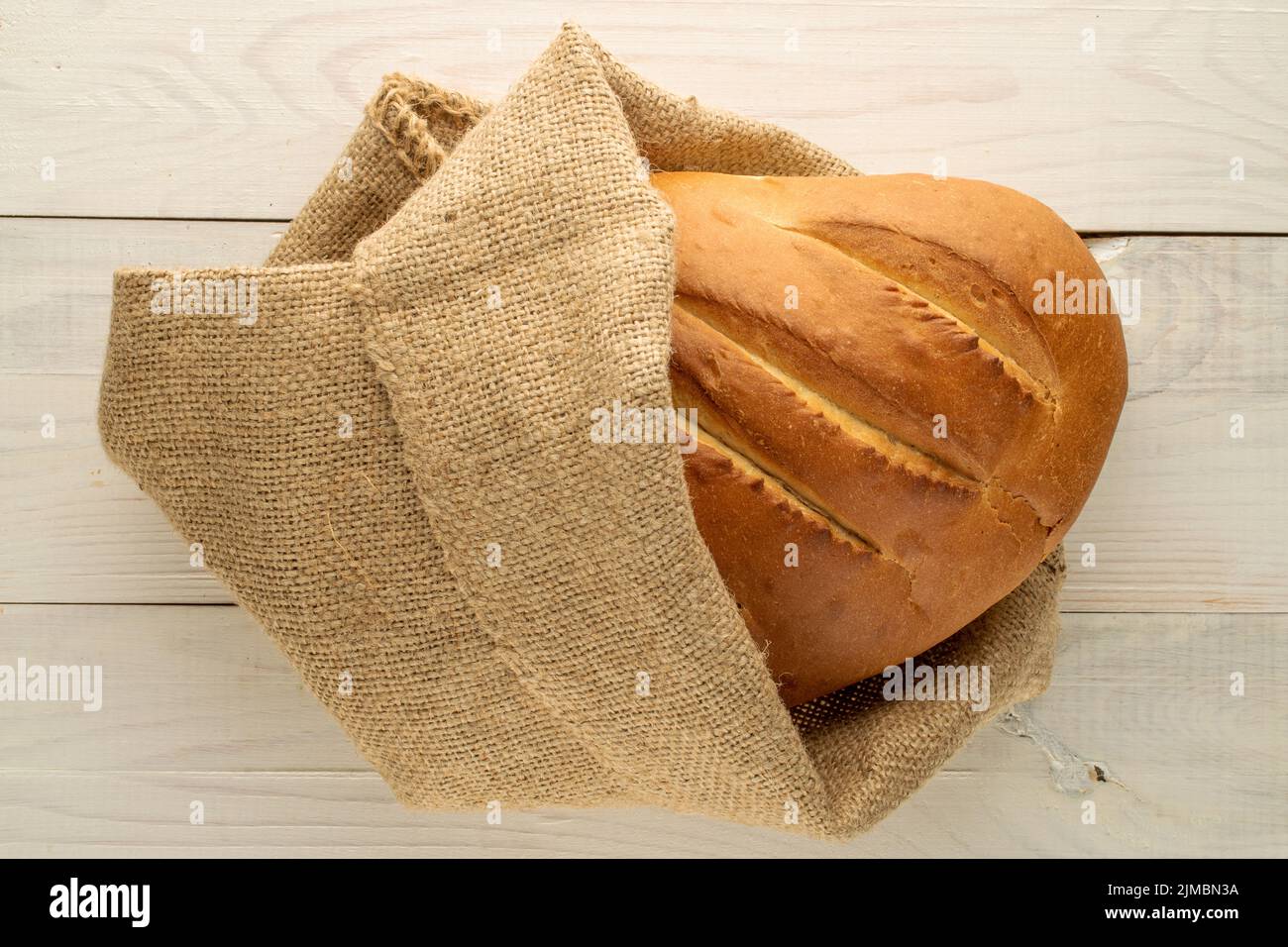 One fragrant fresh loaf in a jute bag on a wooden table, close-up, top ...