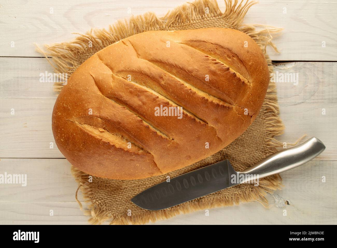 One fragrant fresh loaf with a jute napkin and a knife on a wooden ...