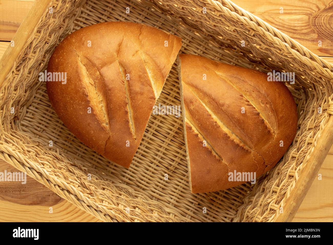 Two halves of a fragrant fresh long loaf in a straw basket on a wooden ...