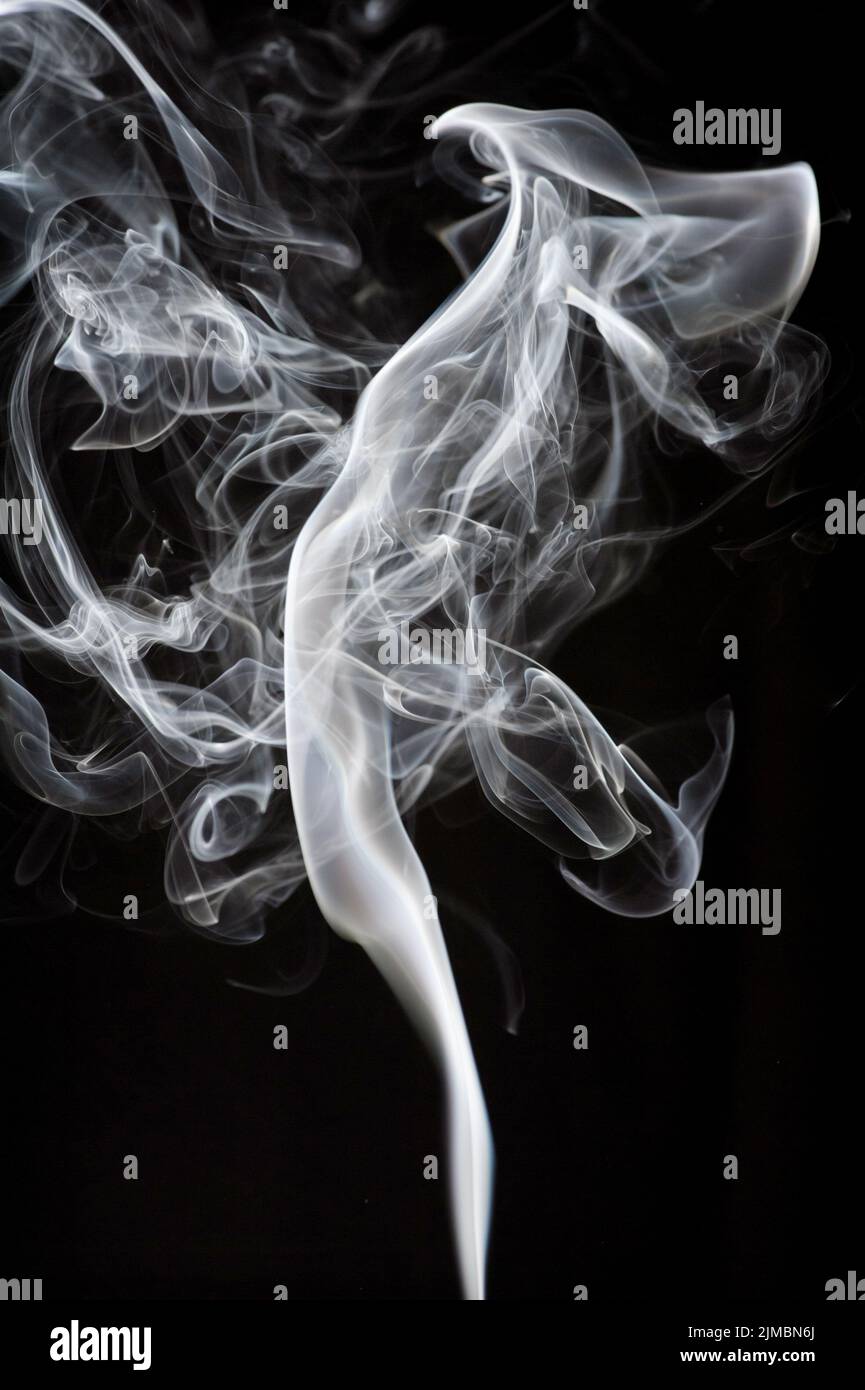 Puffs and curls of white smoke against a black background rising from a ...