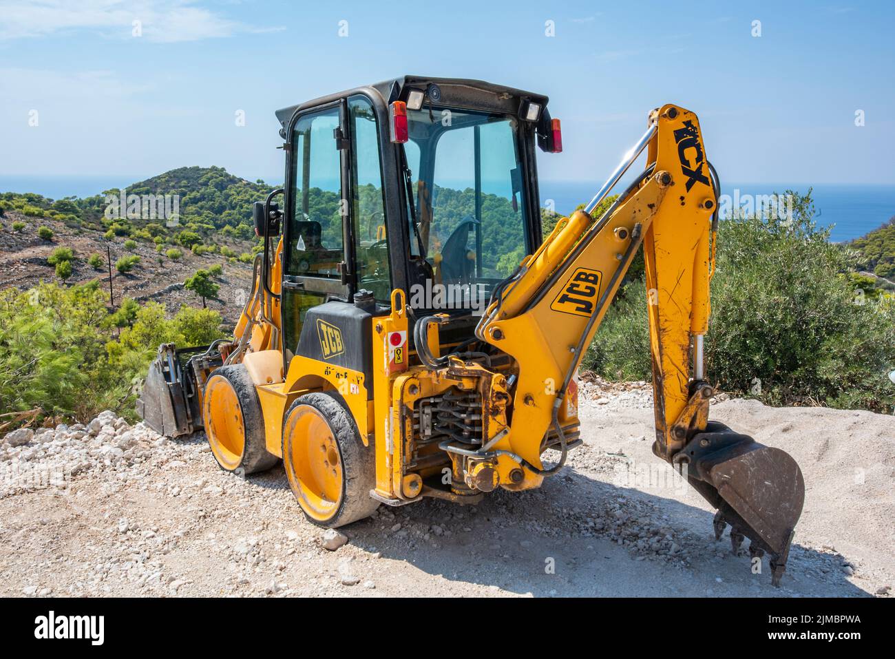 small JCB digger with bucket on a building site on the coast on a hill ...