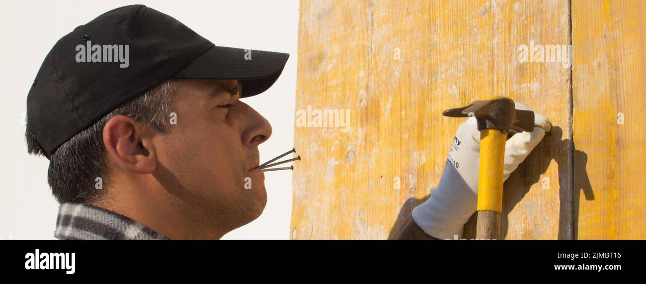 Image of a construction worker with hat and nails between his lips who ...