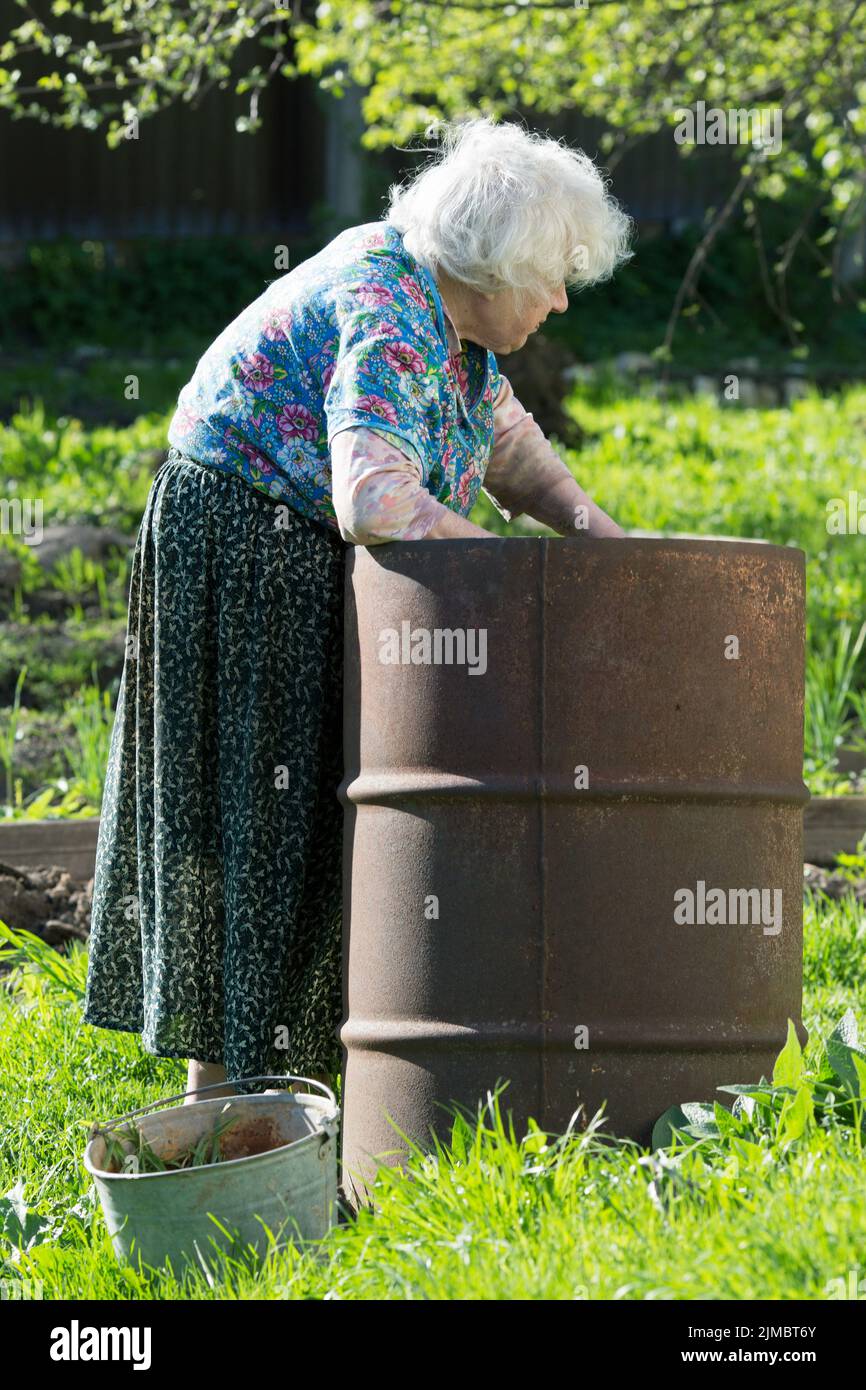 Old woman in the garden at an iron barrel with water Stock Photo - Alamy
