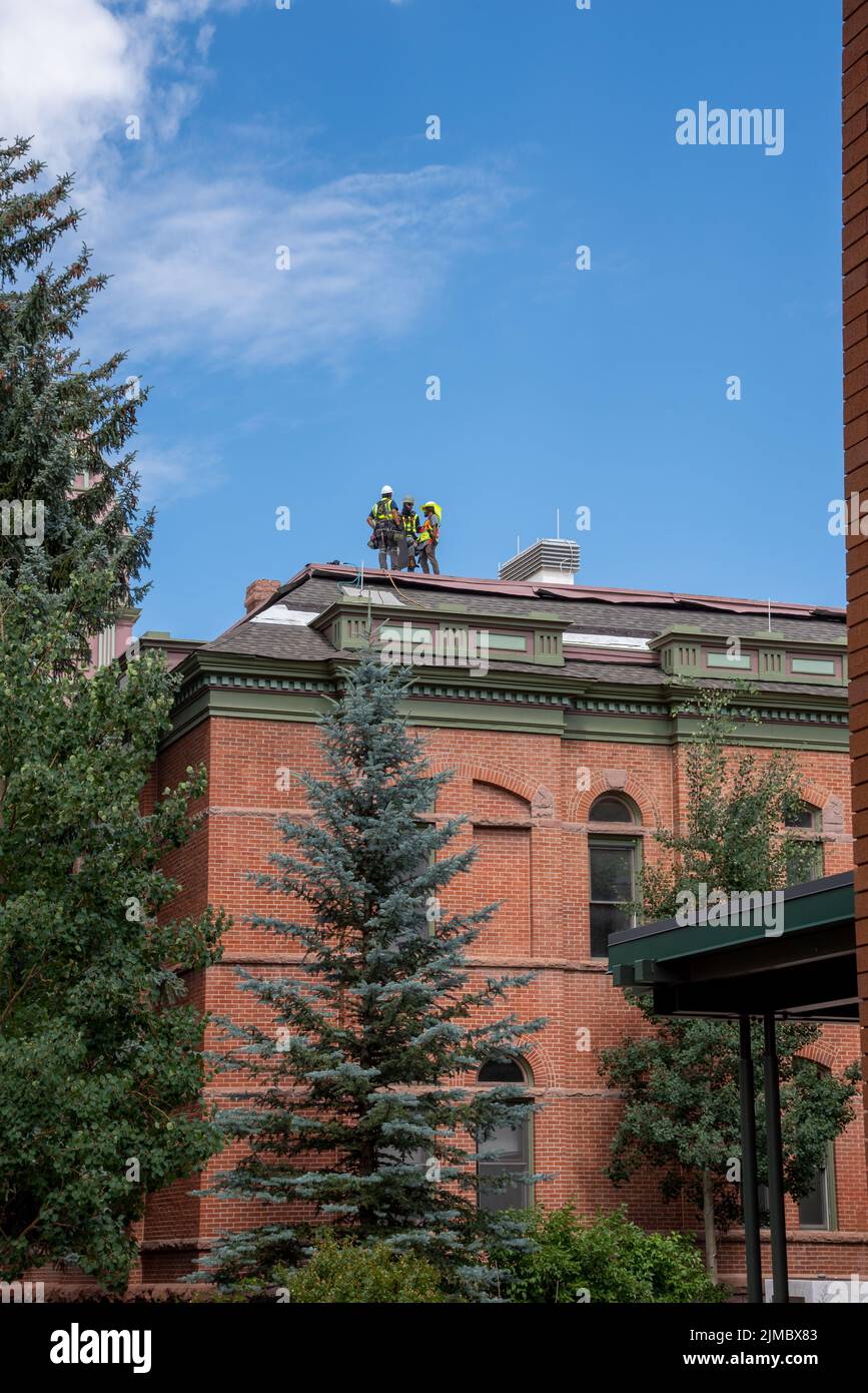 Construction workers stand on the mansard roof of the red brick Pitkin ...