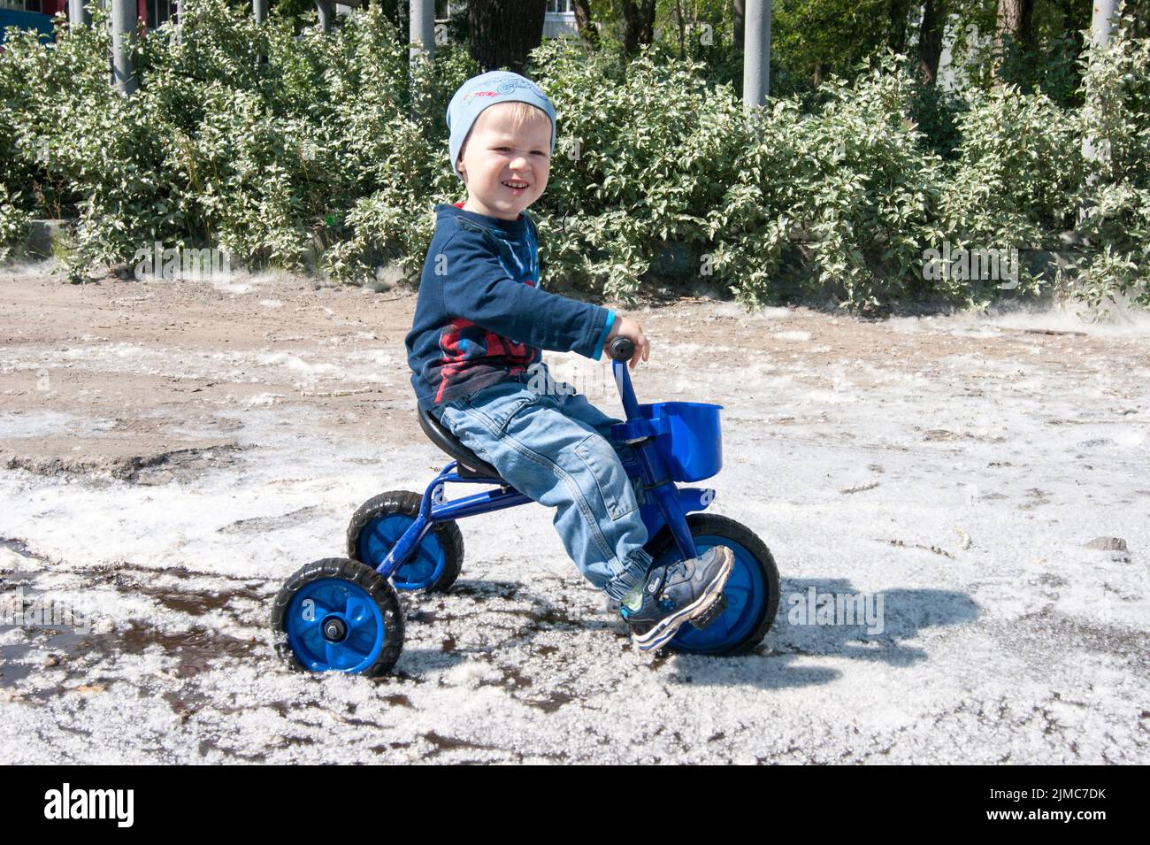 A blond-haired boy in blue rides a small tricycle in a puddle ...