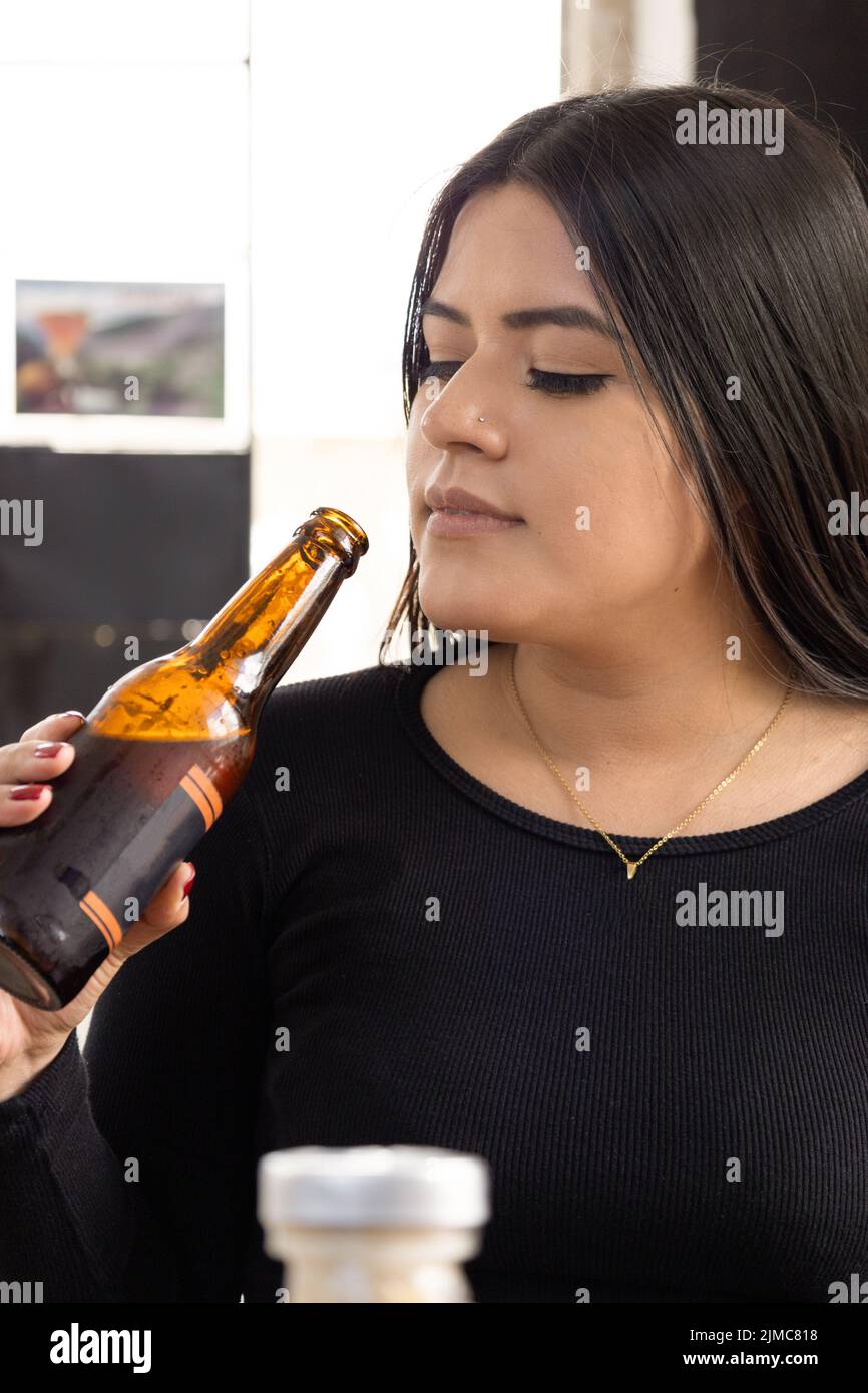 young latin woman holding and drinking a bottle of beer, she has long ...