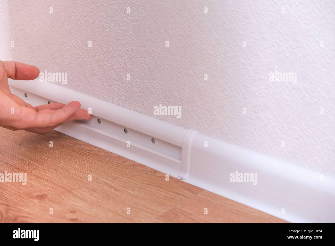 A man installs a floor skirting board. Fixing the plastic skirting ...