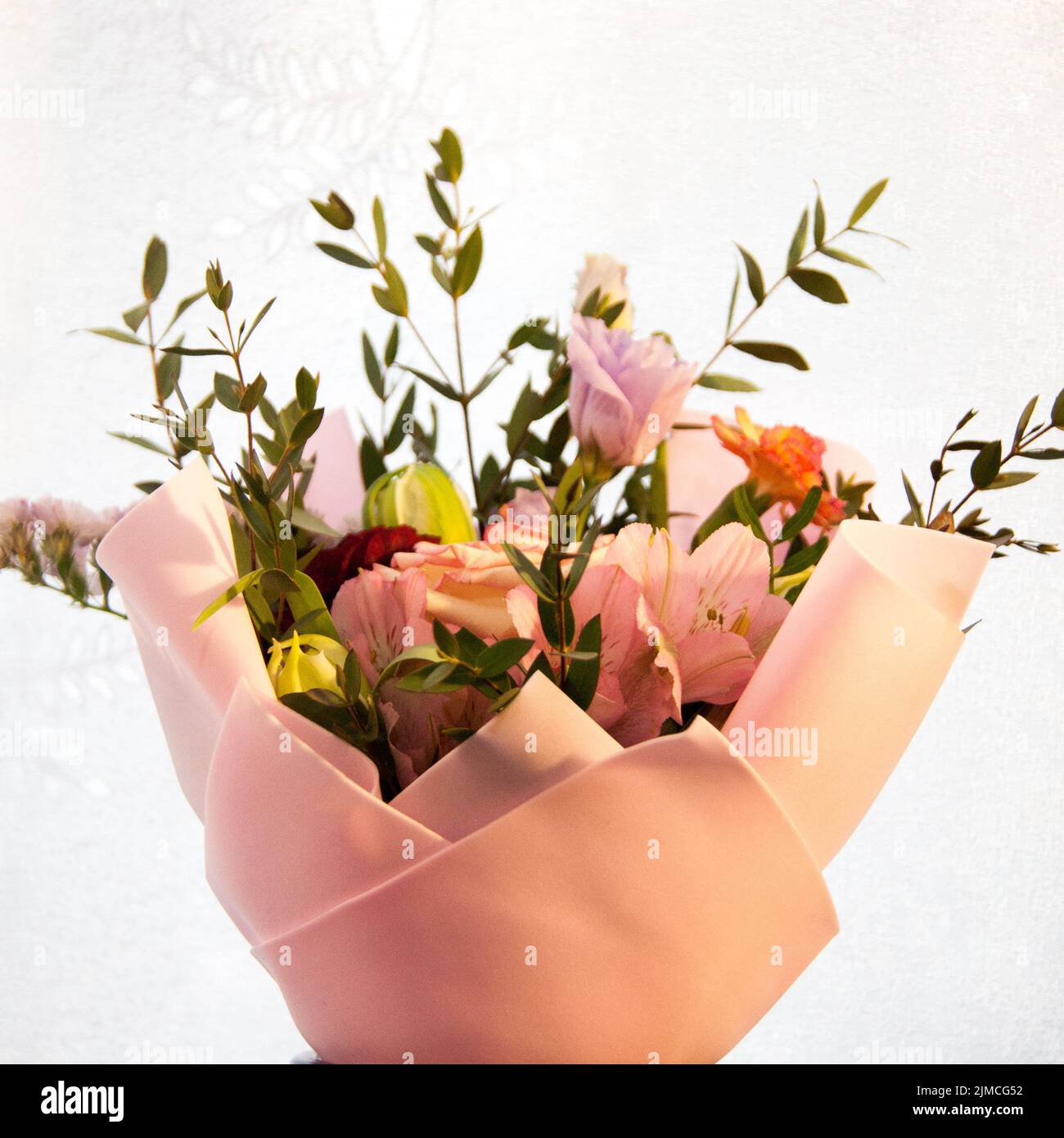 A delicate bouquet of different flowers in a light pink wrapper stands ...