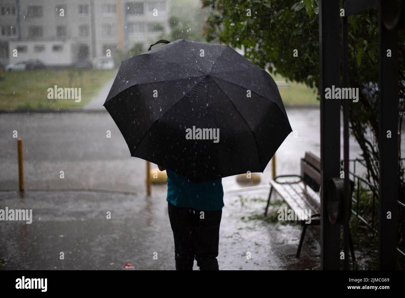 A man with an umbrella under a downpour. A passerby hides from the rain ...