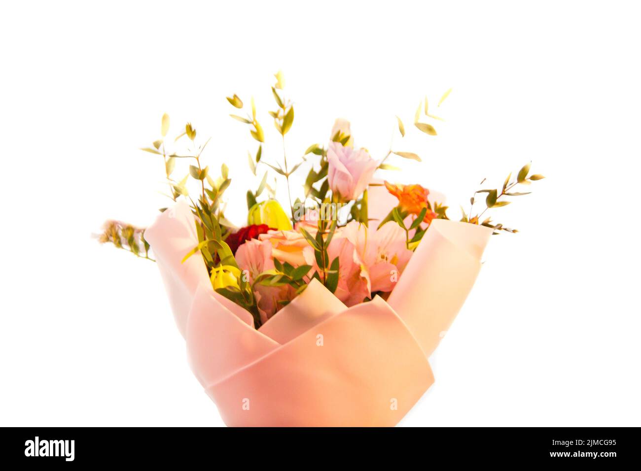 A delicate bouquet of different flowers in a light pink wrapper stands ...