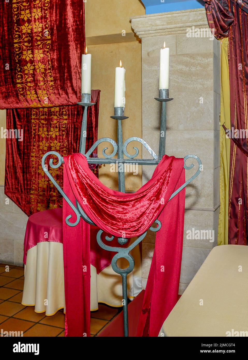 Iron candlestick with three lighted candles adorned with a textured red ...