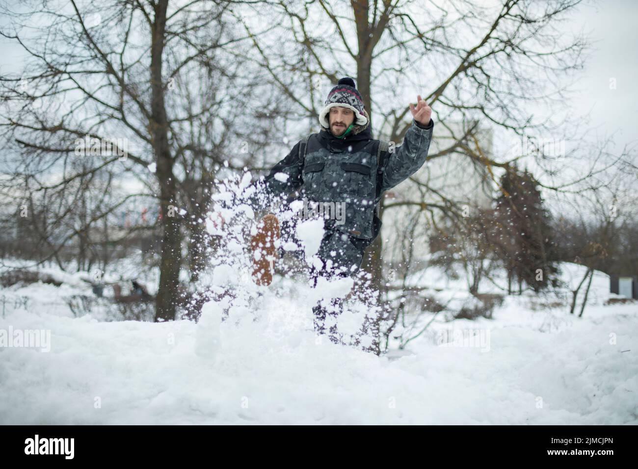 Guy throws snow with his foot. Man in winter in park. Winter fun. Hit ...