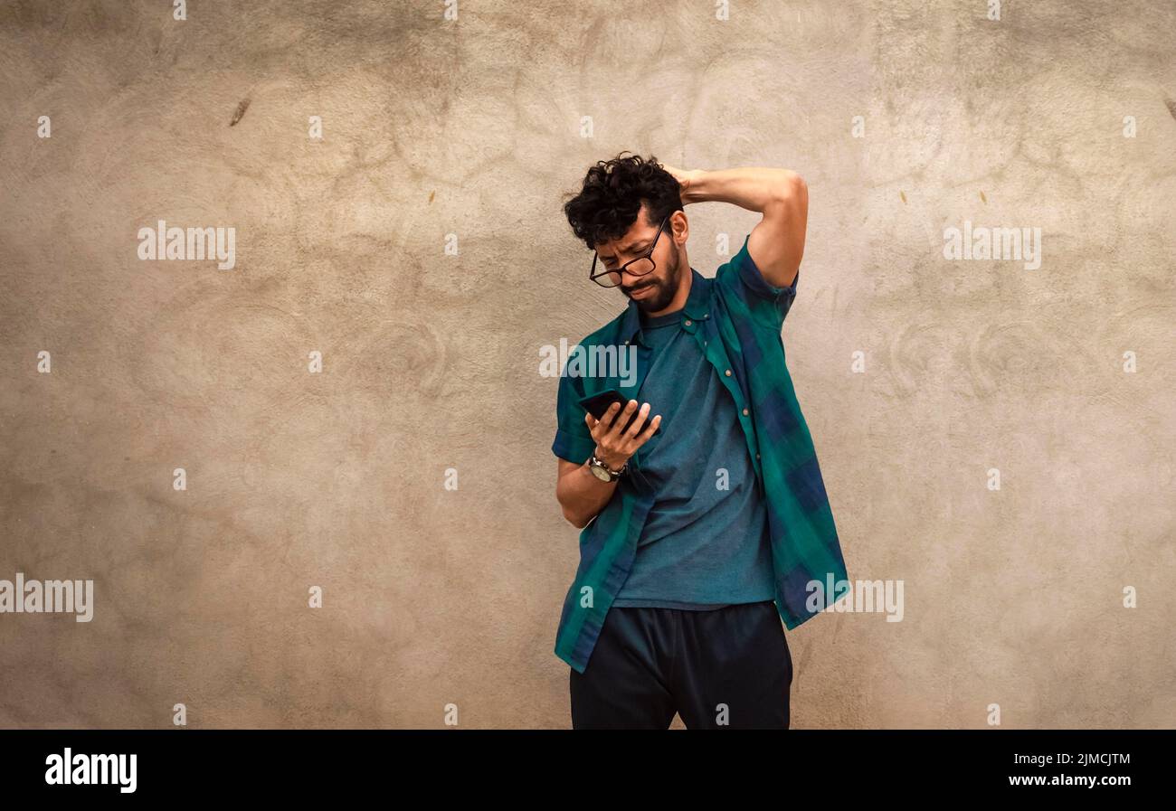 Puzzled teenager scratching his head while checking his cell phone ...