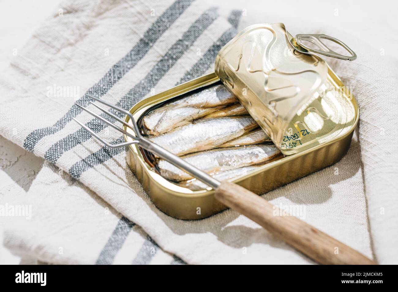 Top view of a can of sardines open in half on a tablecloth on white ...