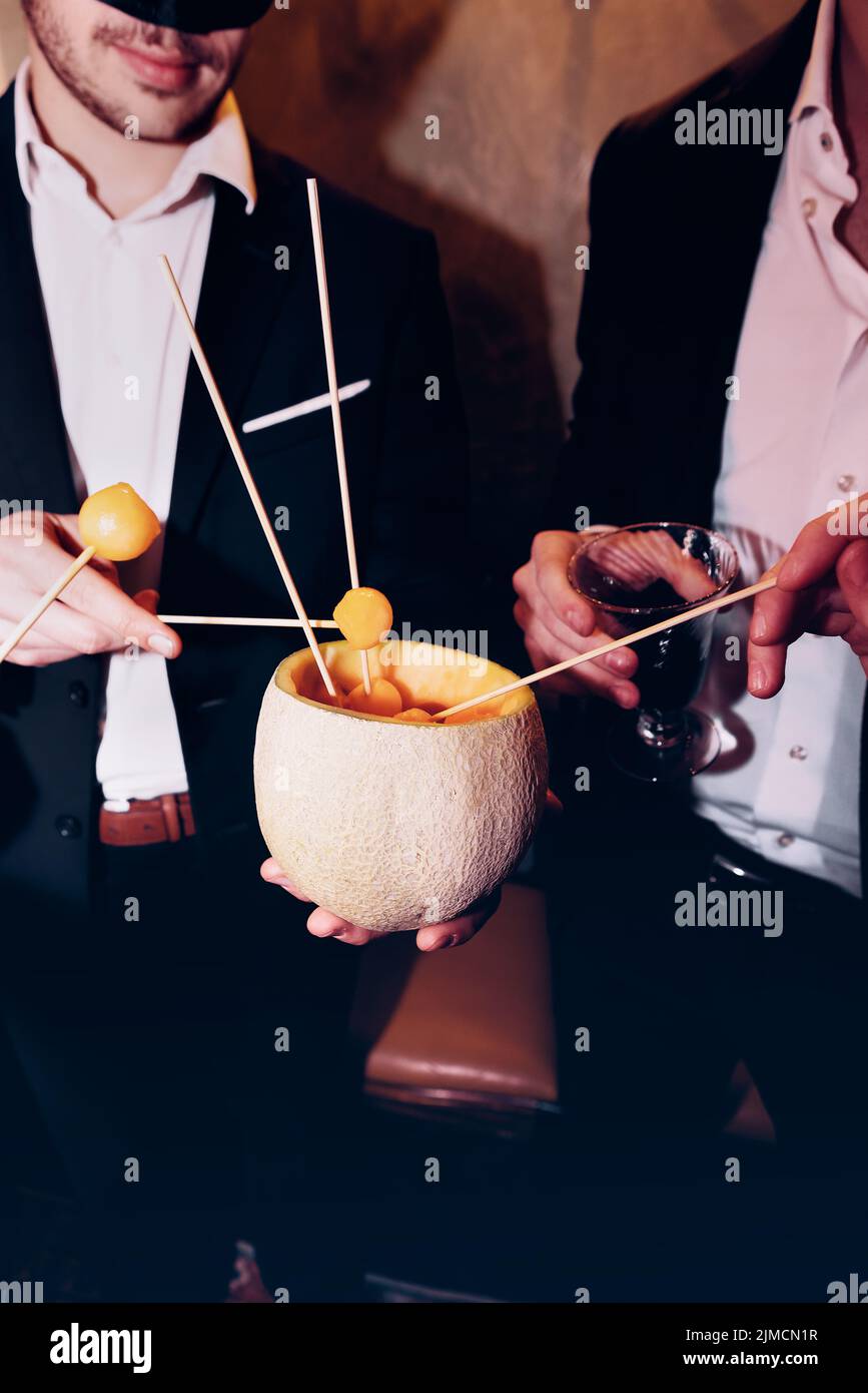 Crop anonymous male friends in elegant clothes eating tasty fresh melon ...