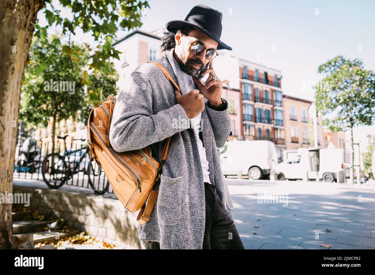 Trendy Hispanic man with leather backpack leaning on fence and ...