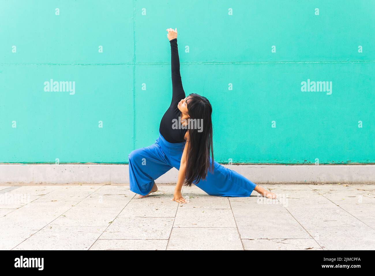 Full body graceful young ethnic female raising arm and touching ground ...