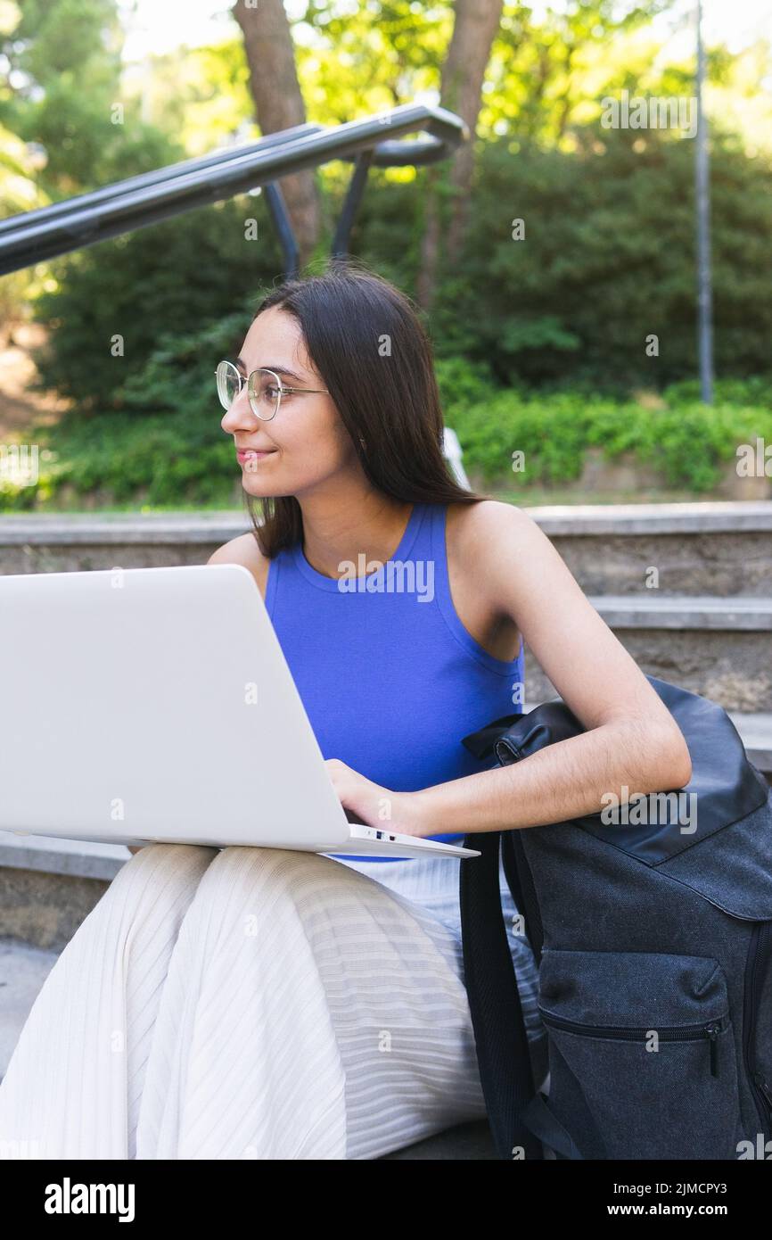 Focused female student typing on netbook while doing homework on stone ...